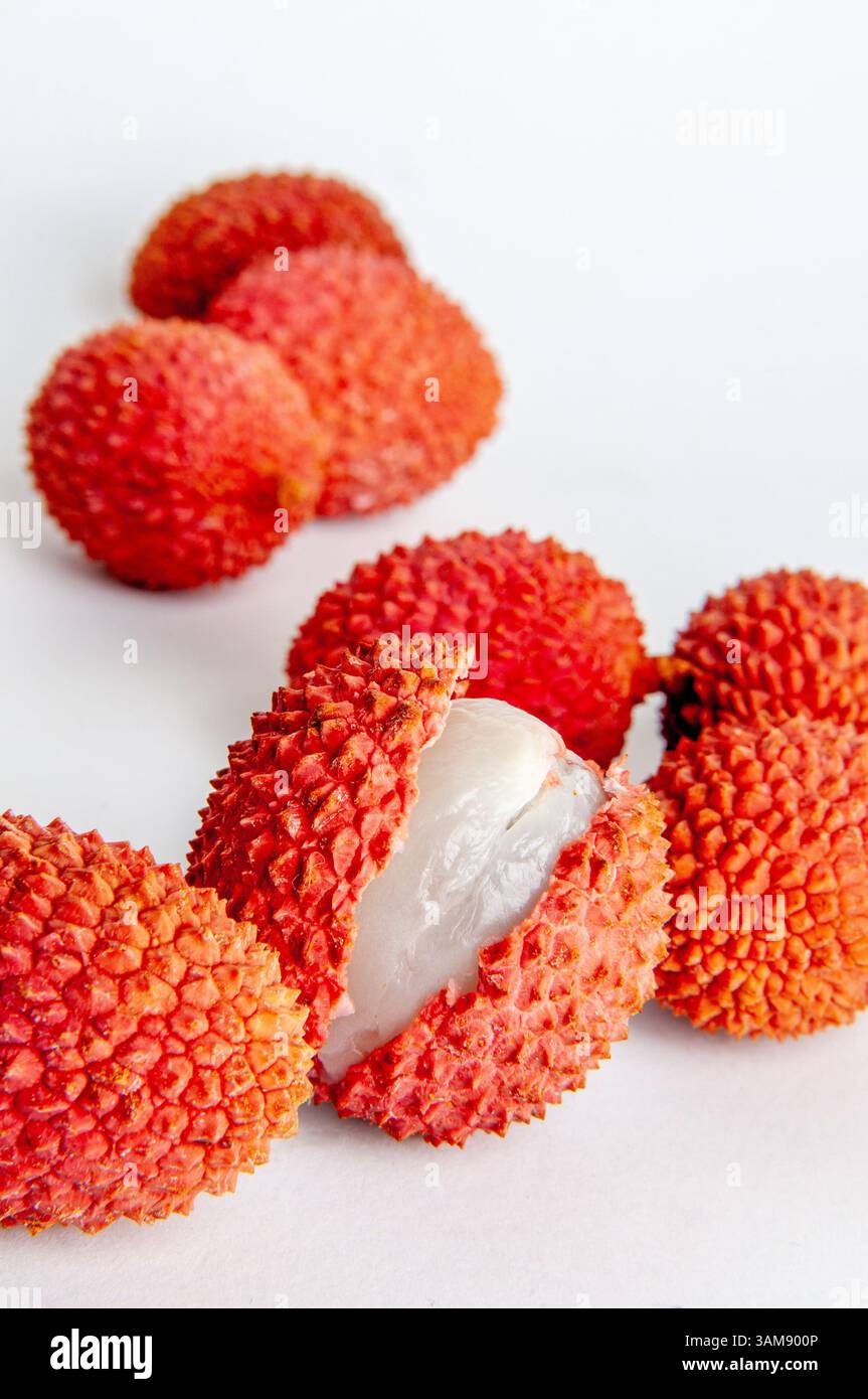 Vibrant red lychees are scattered, revealing a few cut-open fruits ...