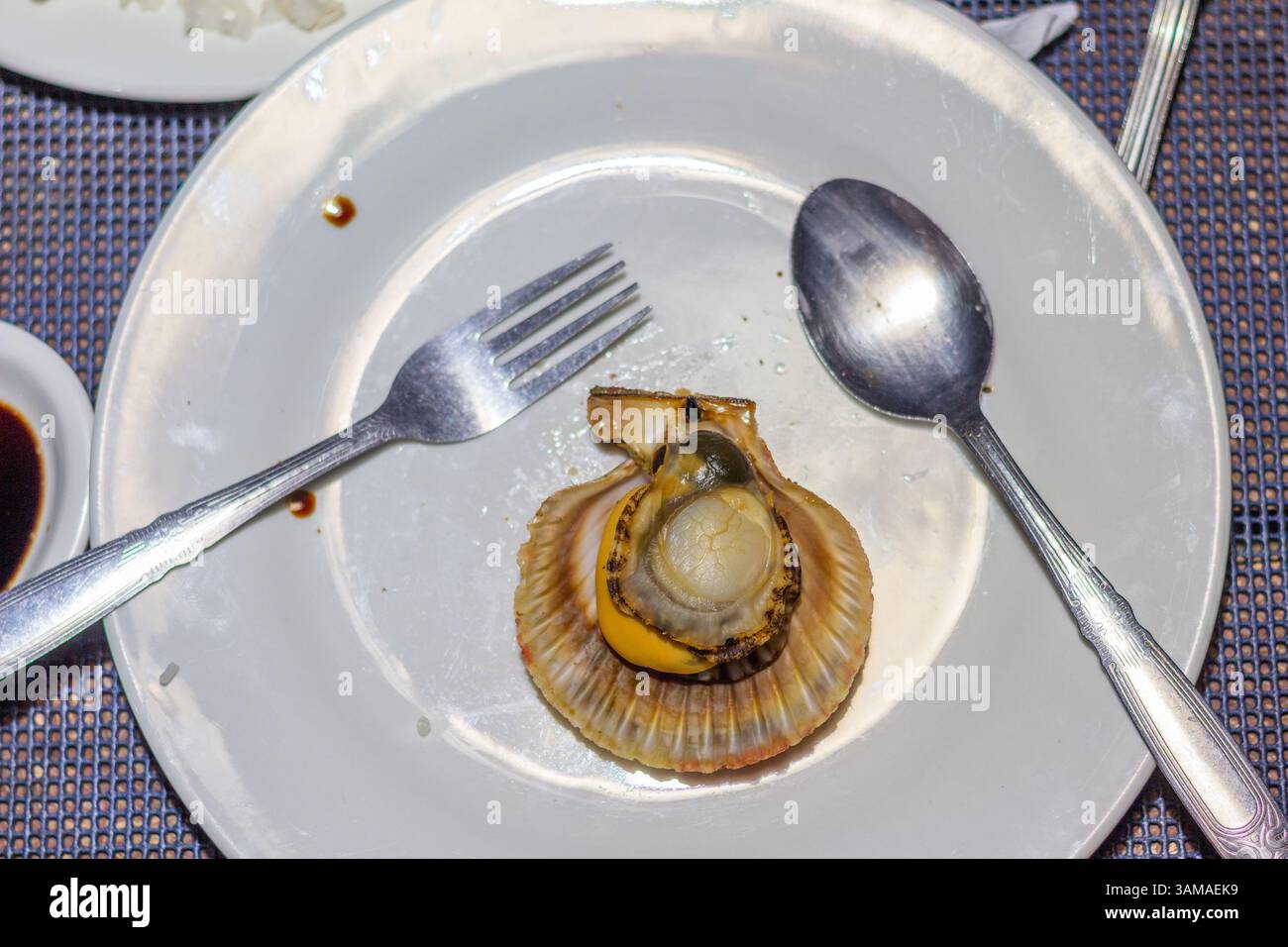 A steamed scallop shell on a plate with spoon and fork at a dinner ...