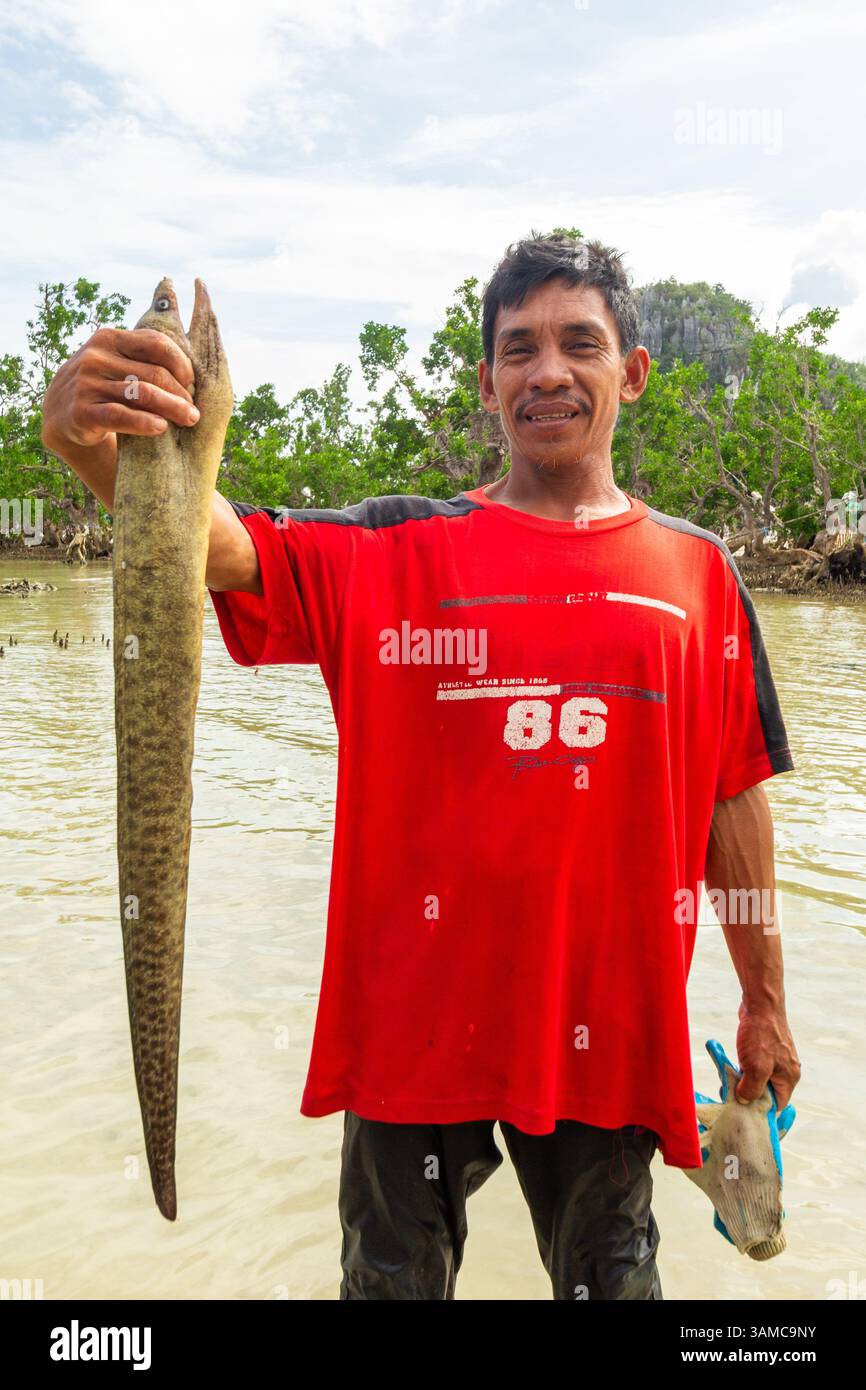 A middle-aged Filipino fisherman in a red shirt holds a freshly caught ...