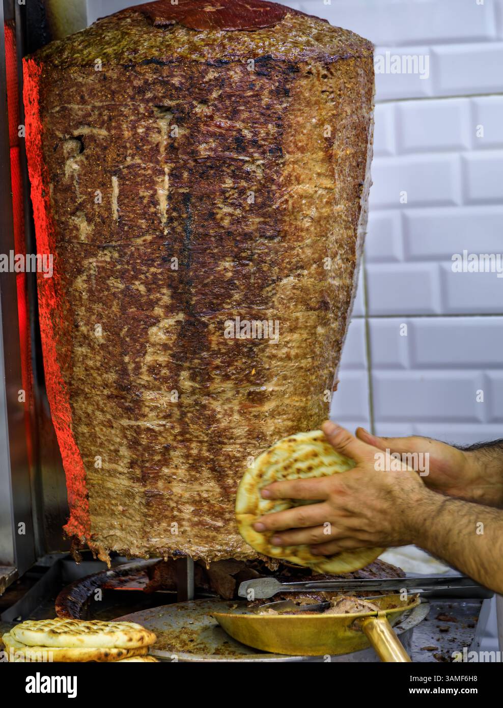 The doner kebab meat cooks on a vertical spit as it's being sliced for ...