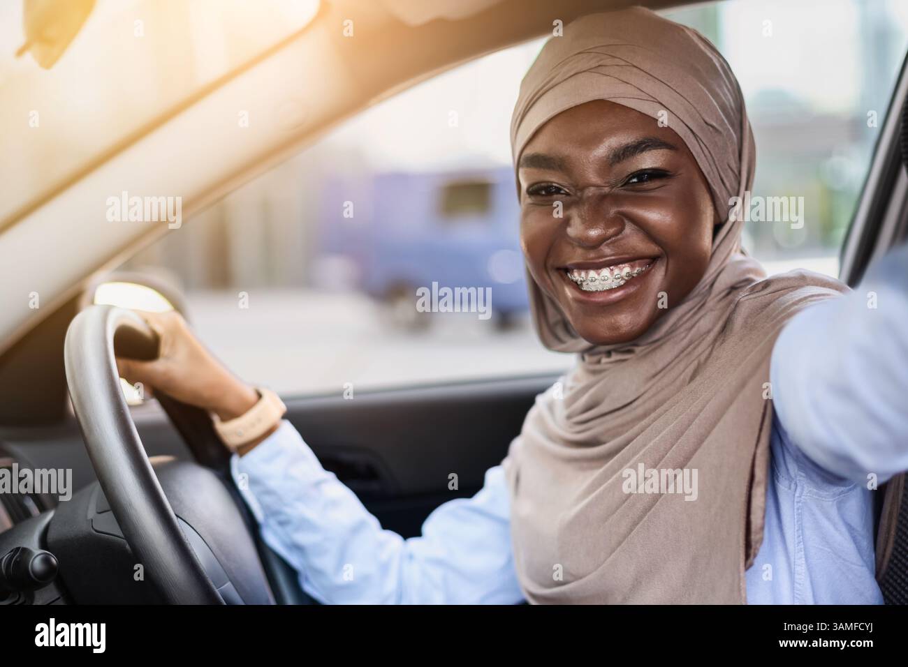Car Selfie. Cheerful black muslim woman taking self-portrait in her new ...