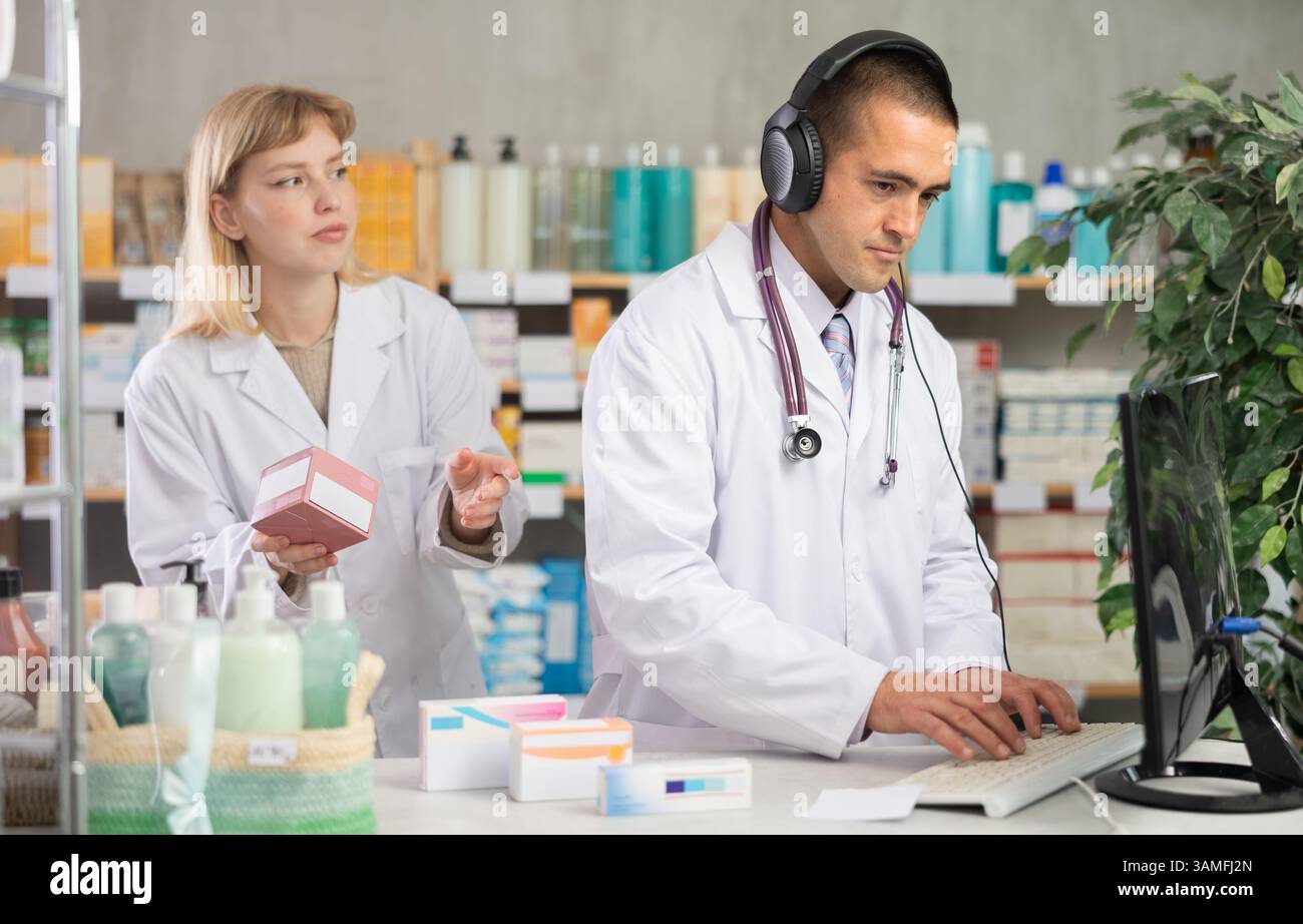 Man pharmacist works at computer using headset, girl assistant in ...
