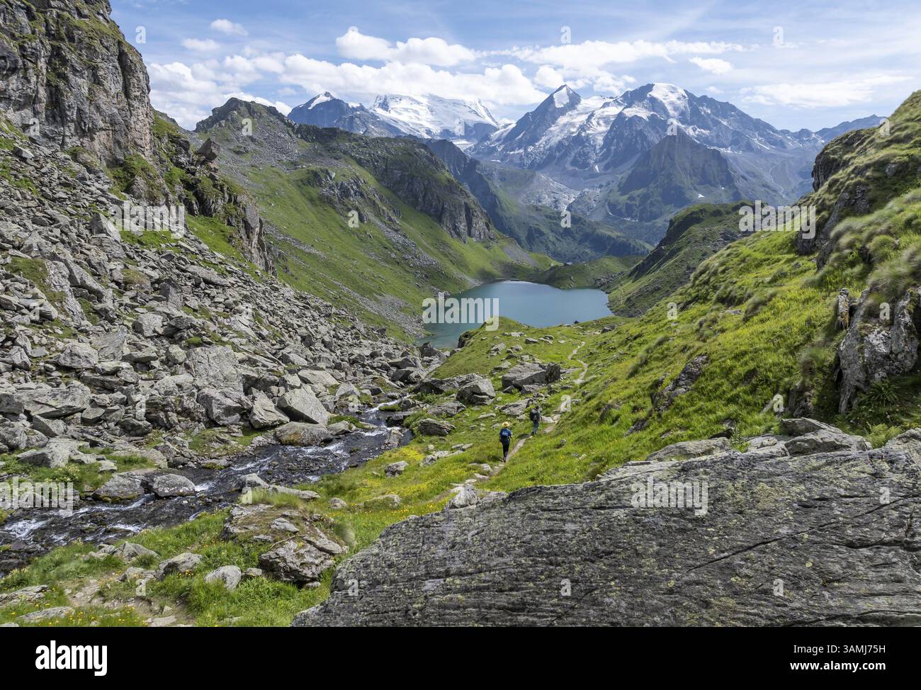 Hiker in front of mountain stream and mountain lake Lac de Louvie with ...