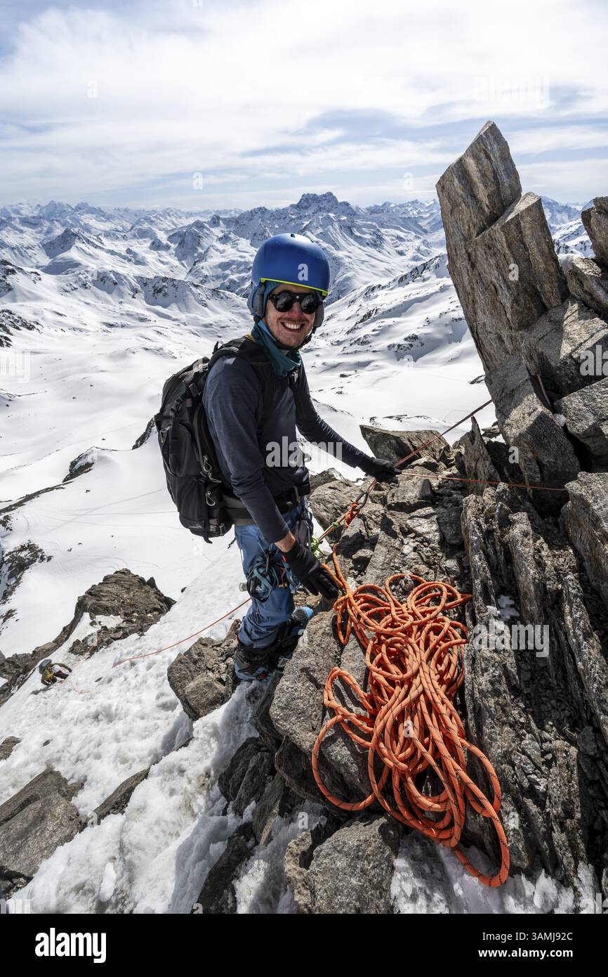 Mountaineer belaying with rope, climbing up a steep snow slope ...