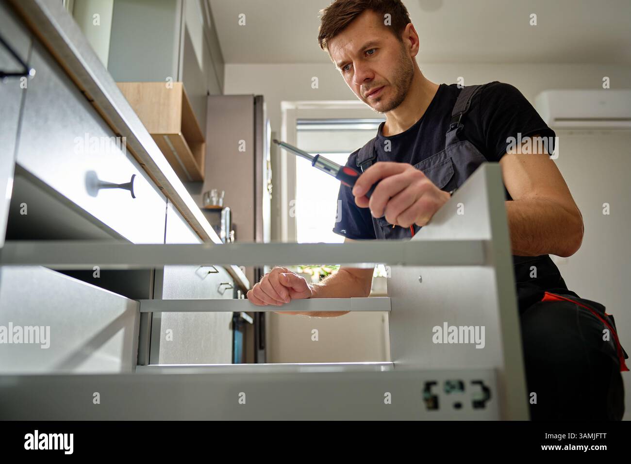 Man assembling kitchen drawer in modern cabinet using screwdriver ...