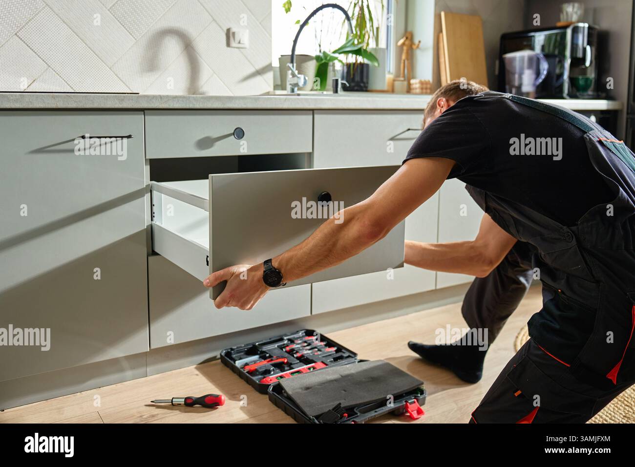 Man assembling kitchen drawer in modern cabinet using screwdriver ...