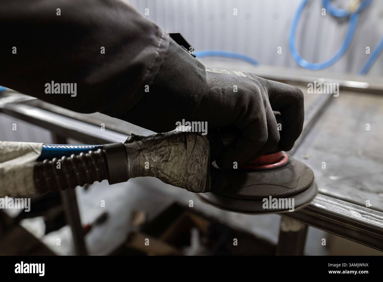 A worker's gloved hand uses a power sander to smooth the joints of a ...