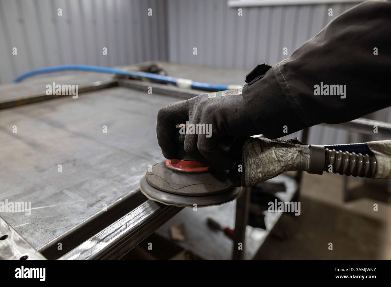 A worker's gloved hand uses a power sander to smooth the joints of a ...