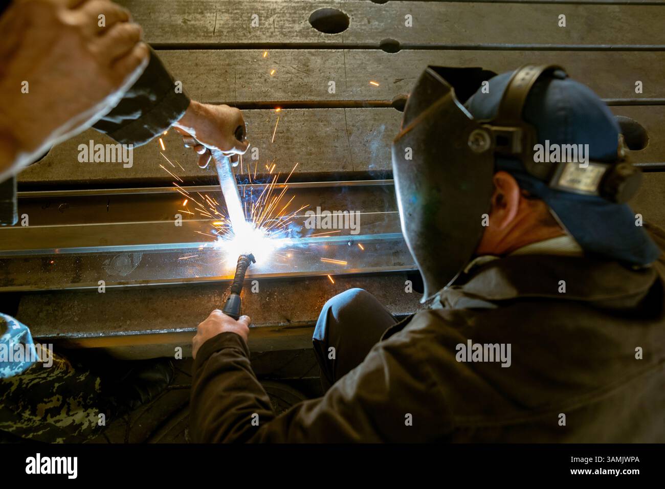 A welder, holding the automatic welding head, and an assistant, firmly ...