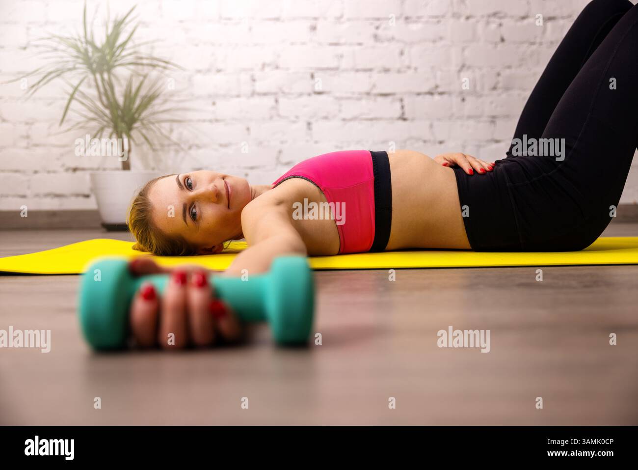 fitness woman laying down on yoga mat with dumbbell in hand in the gym ...