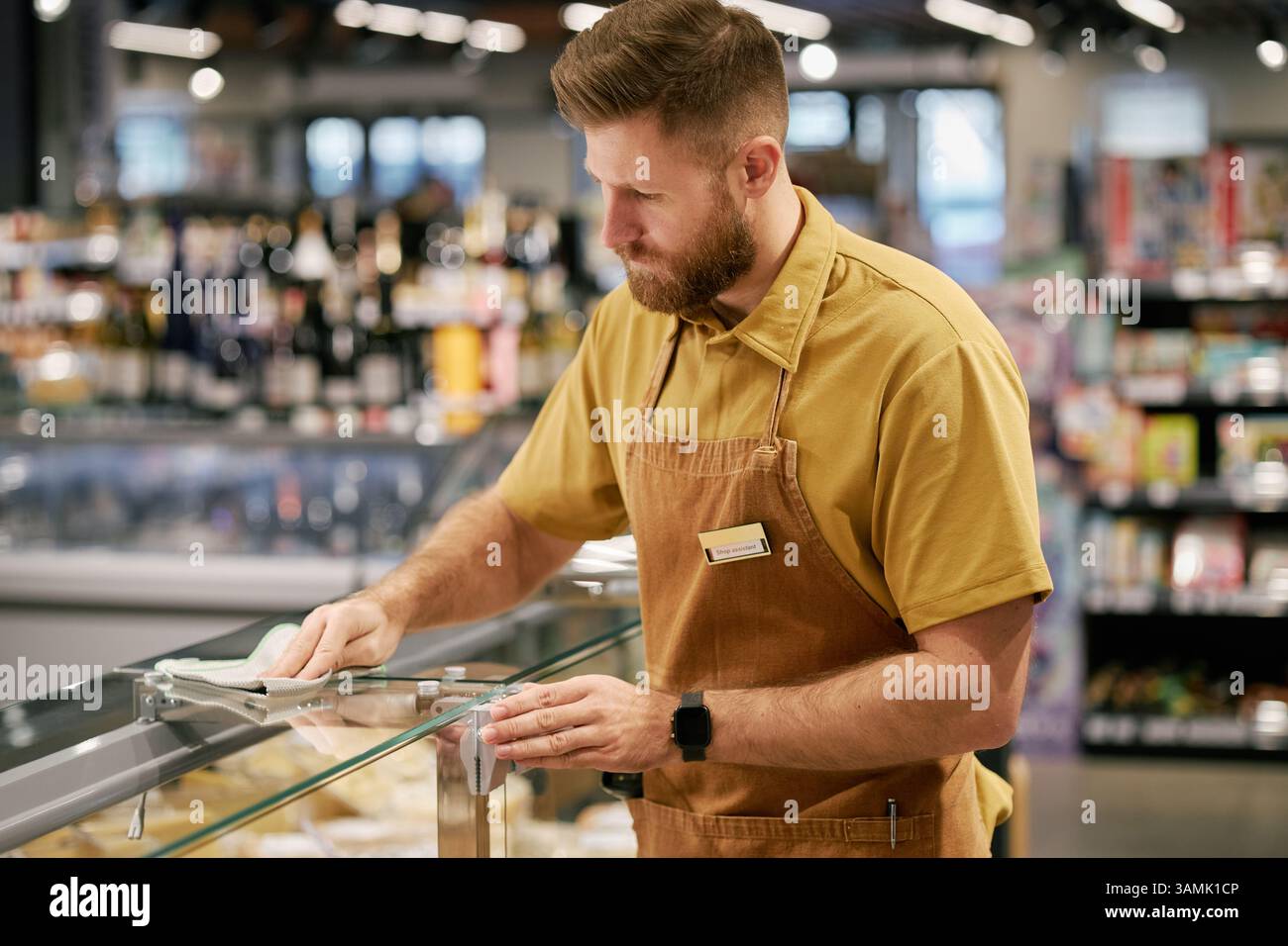 Bearded man with brown hair in uniform arranging items at grocery store ...