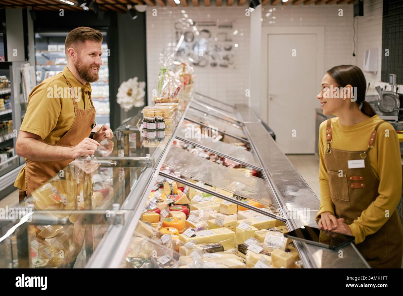 Male shop assistant with beard and female customer discussing cheese ...