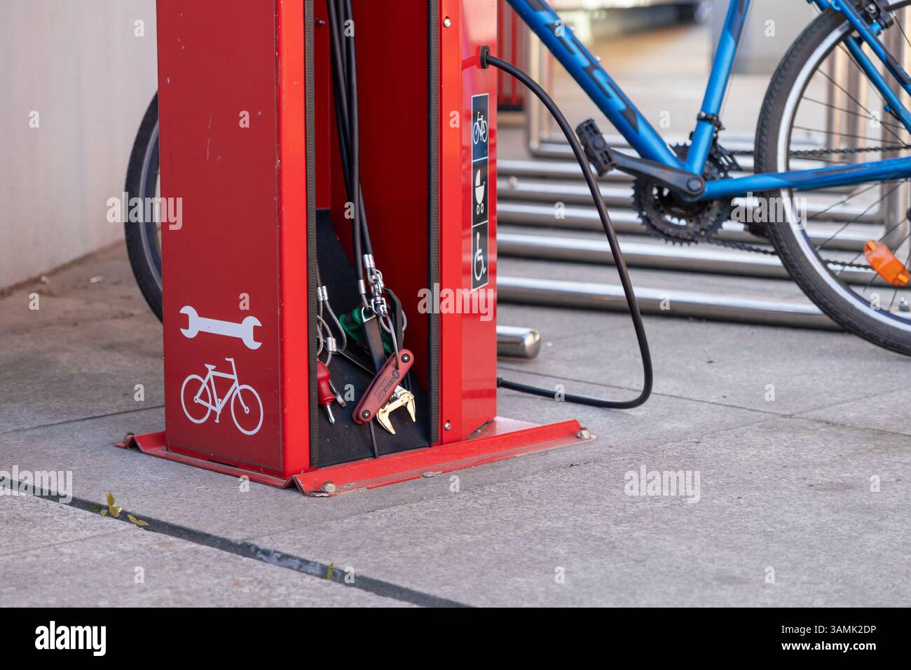 Close-up of urban bike repair station with visible tools and air hose next to a blue bicycle ...