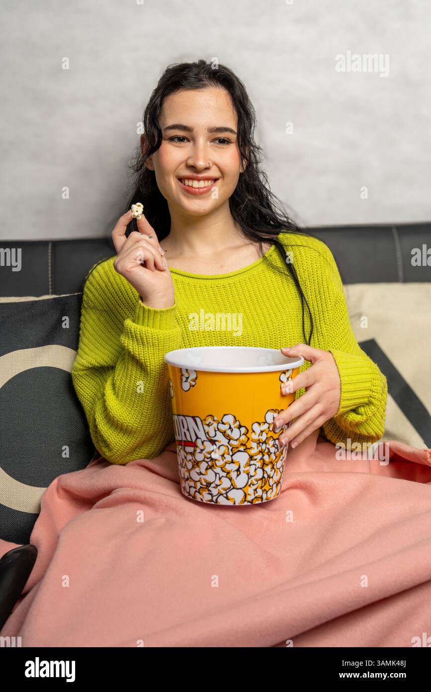 Young woman enjoying a movie night at home, eating popcorn from a ...