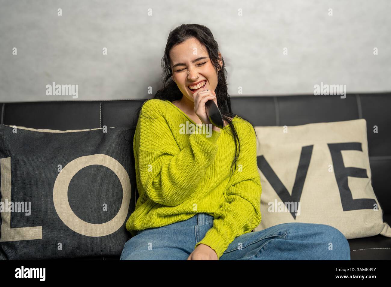 Happy young woman singing karaoke, holding remote control as microphone ...