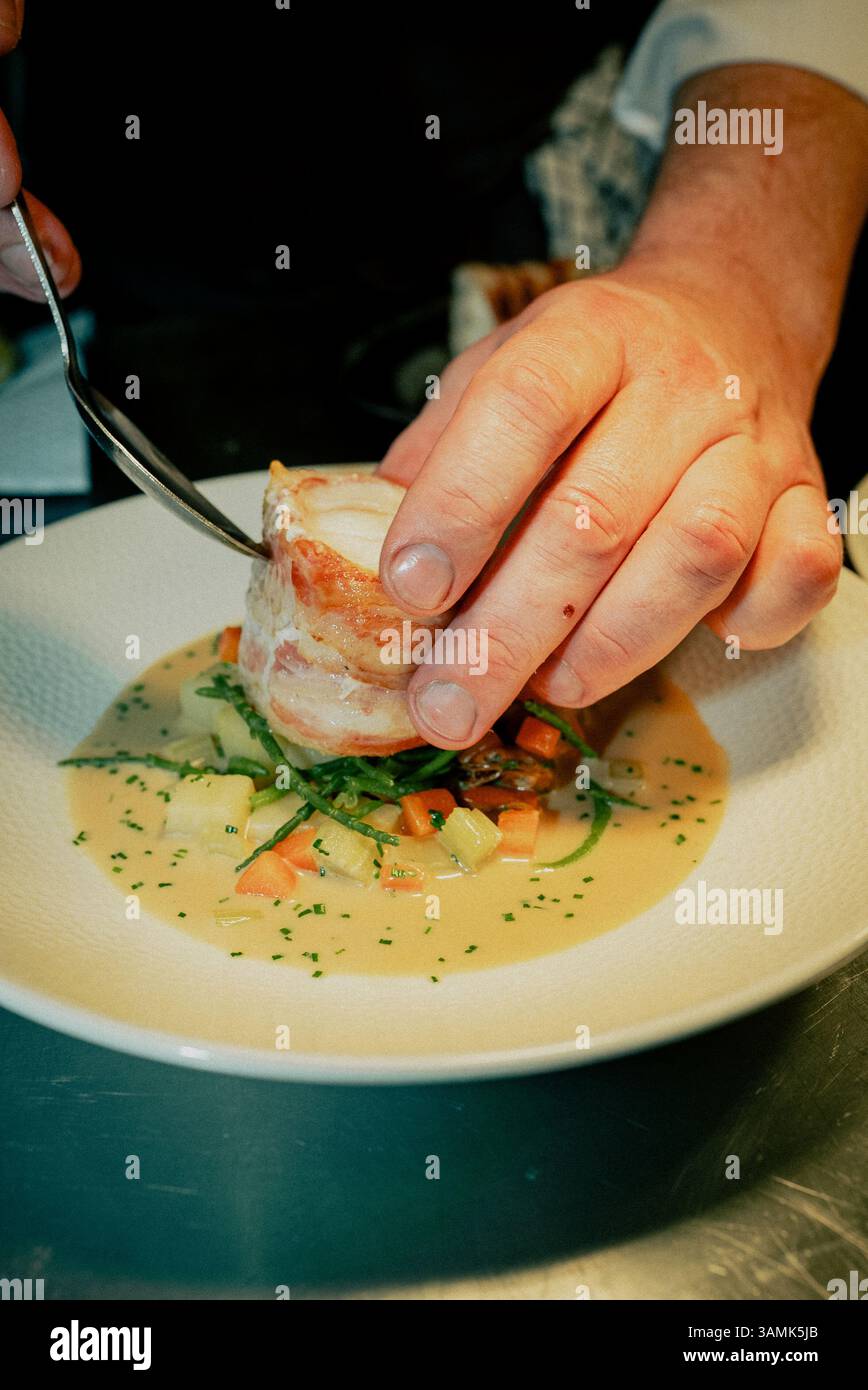 A man is putting food on a plate. The plate has a white background and ...