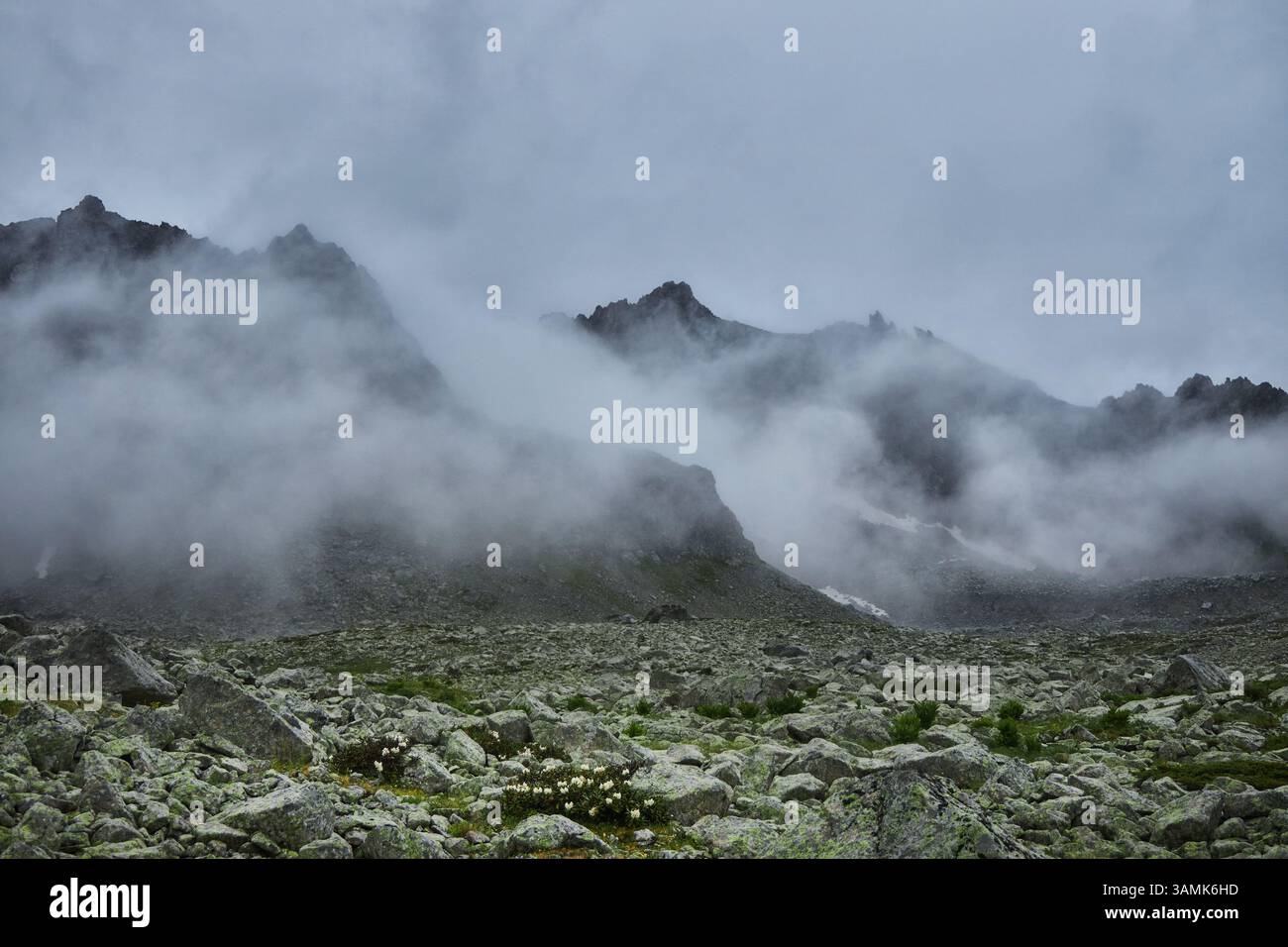 Low-hanging fog swirls around rugged mountain peaks in a remote area ...