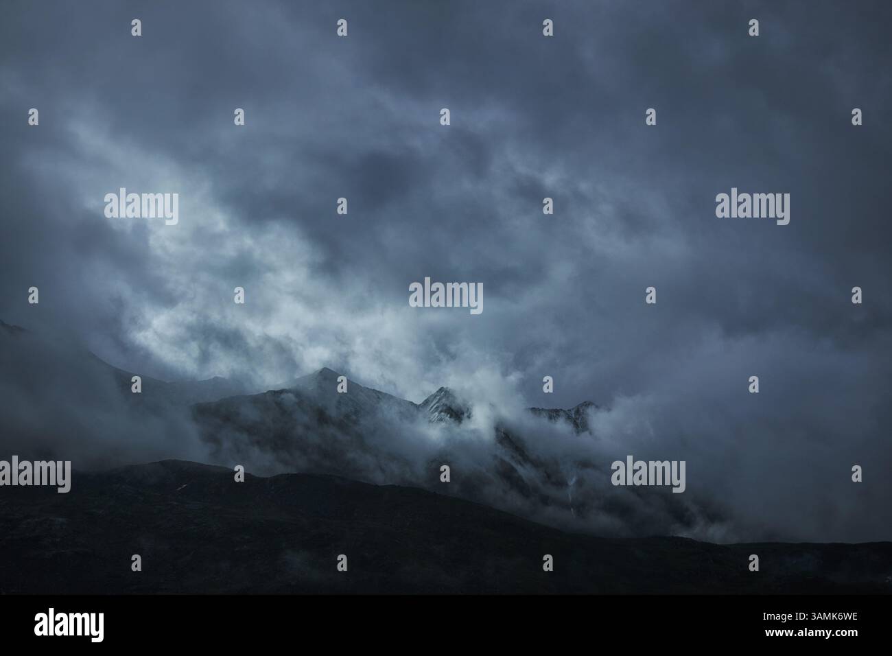 Dark clouds swirl around rugged mountain peaks, partially obscured by ...