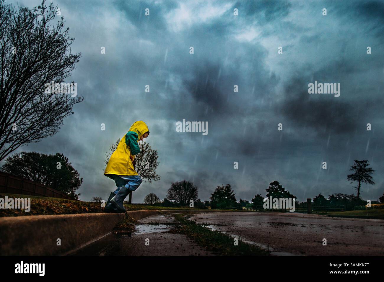 Boy jumping off curb into rain puddle Stock Photo - Alamy