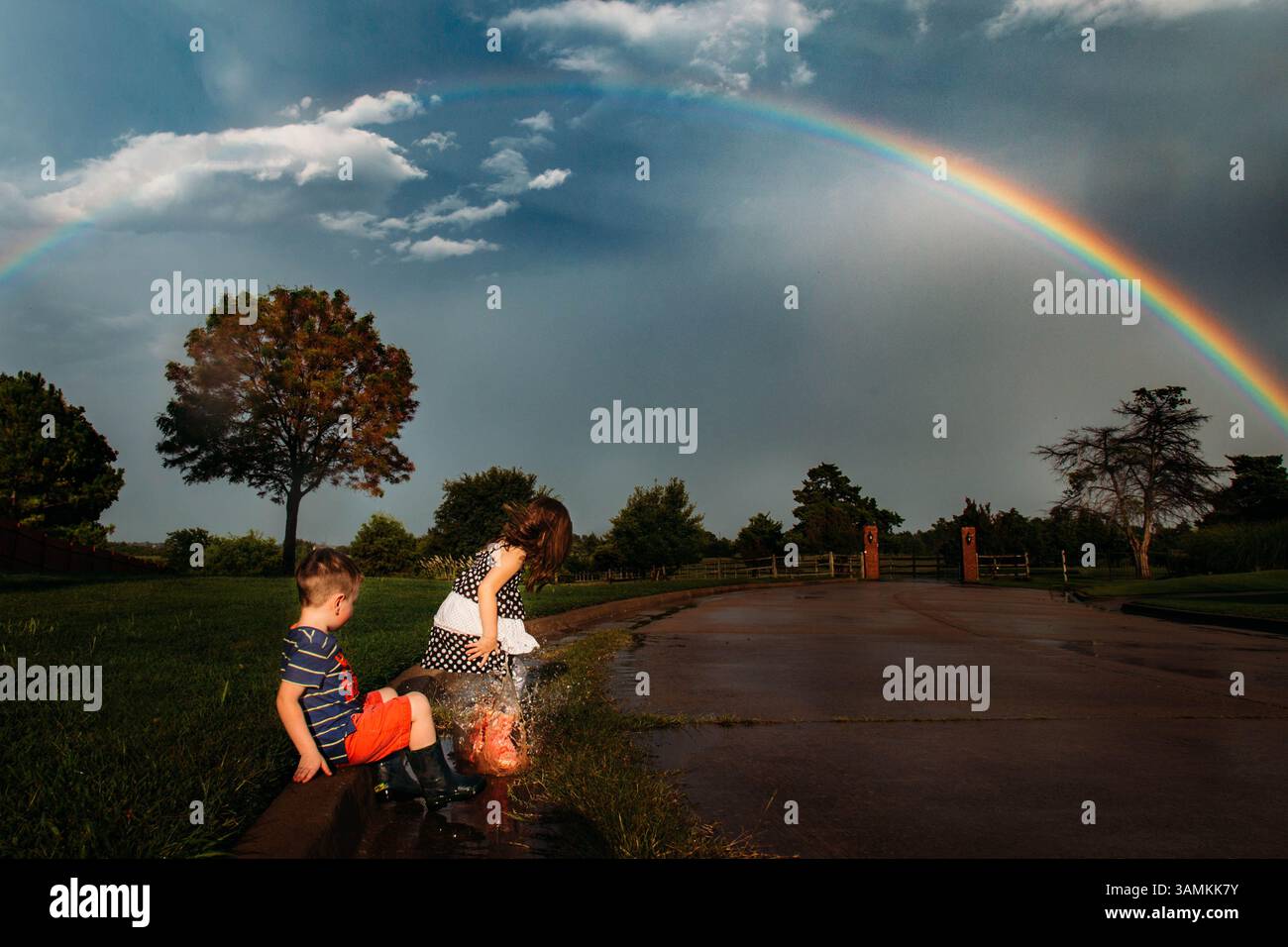 Children jumping in rain puddle with rainbow overhead Stock Photo - Alamy