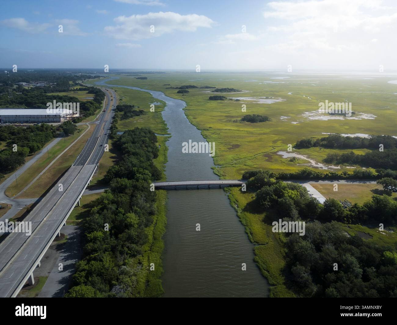Aerial view of serene wetlands with a bridge over a river and a highway ...