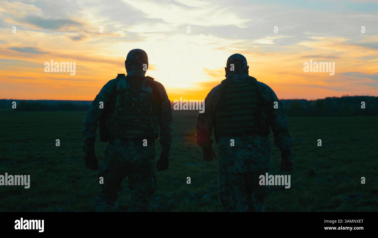 Two soldiers at sunset in open field. Two soldiers in full military gear stand side by side ...