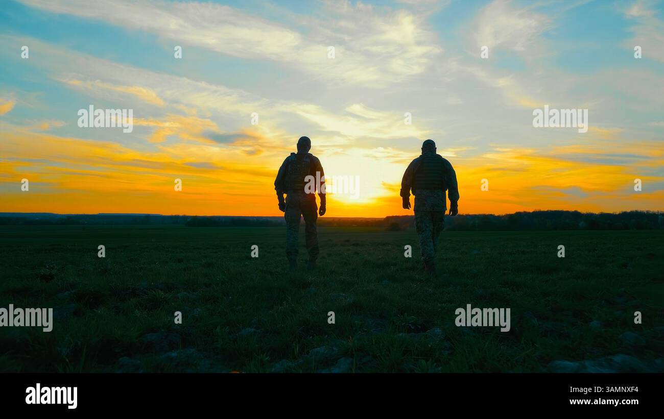 Silhouetted soldiers walking in a field at sunset. Two silhouetted soldiers walk across an open ...