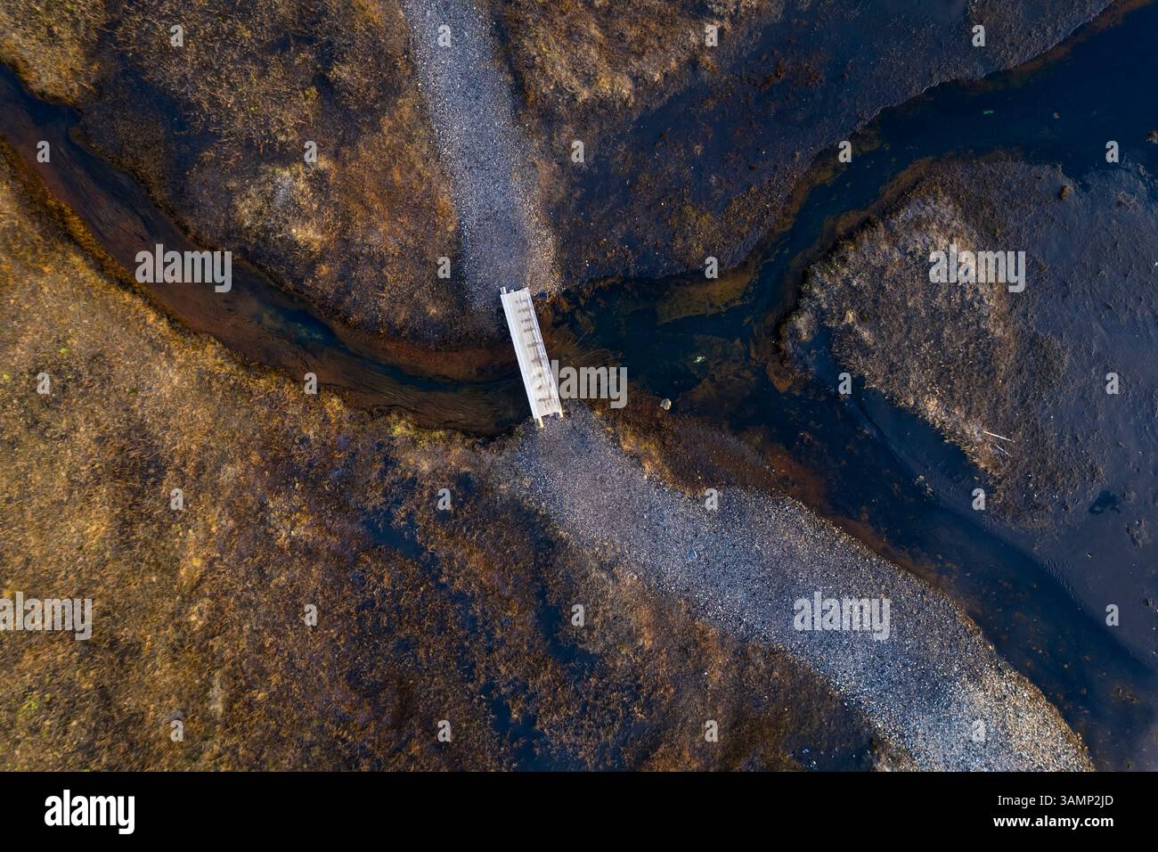 Aerial view of small bridge over stream with gravel path and marsh ...