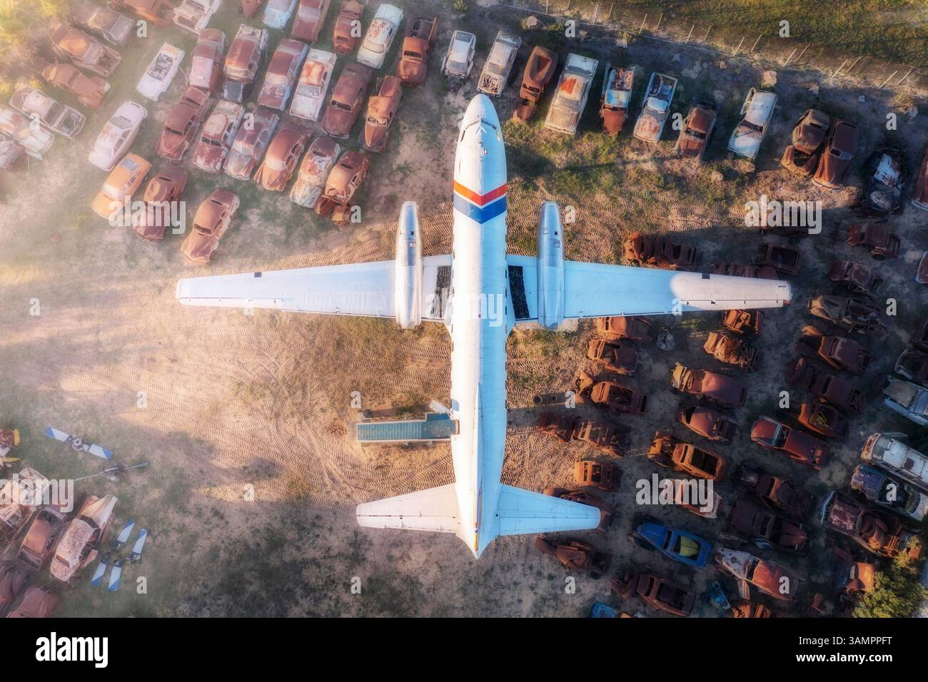 Aerial view of an old airplane parked in a yard of vintage car wrecks ...