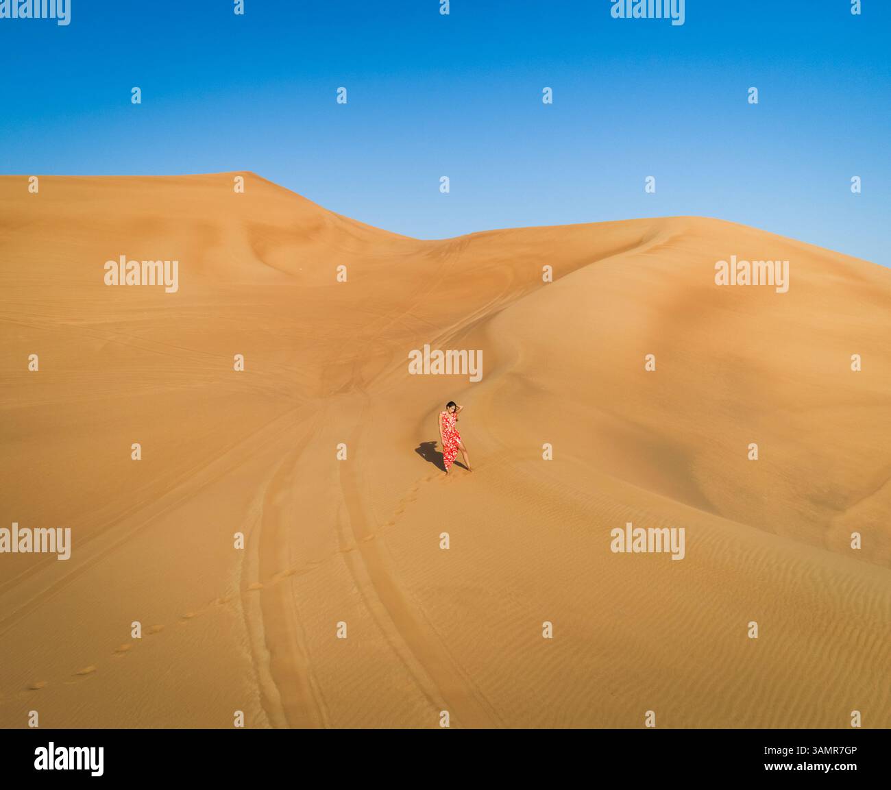 Aerial view of attractive woman using red dress at a desertic landscape ...