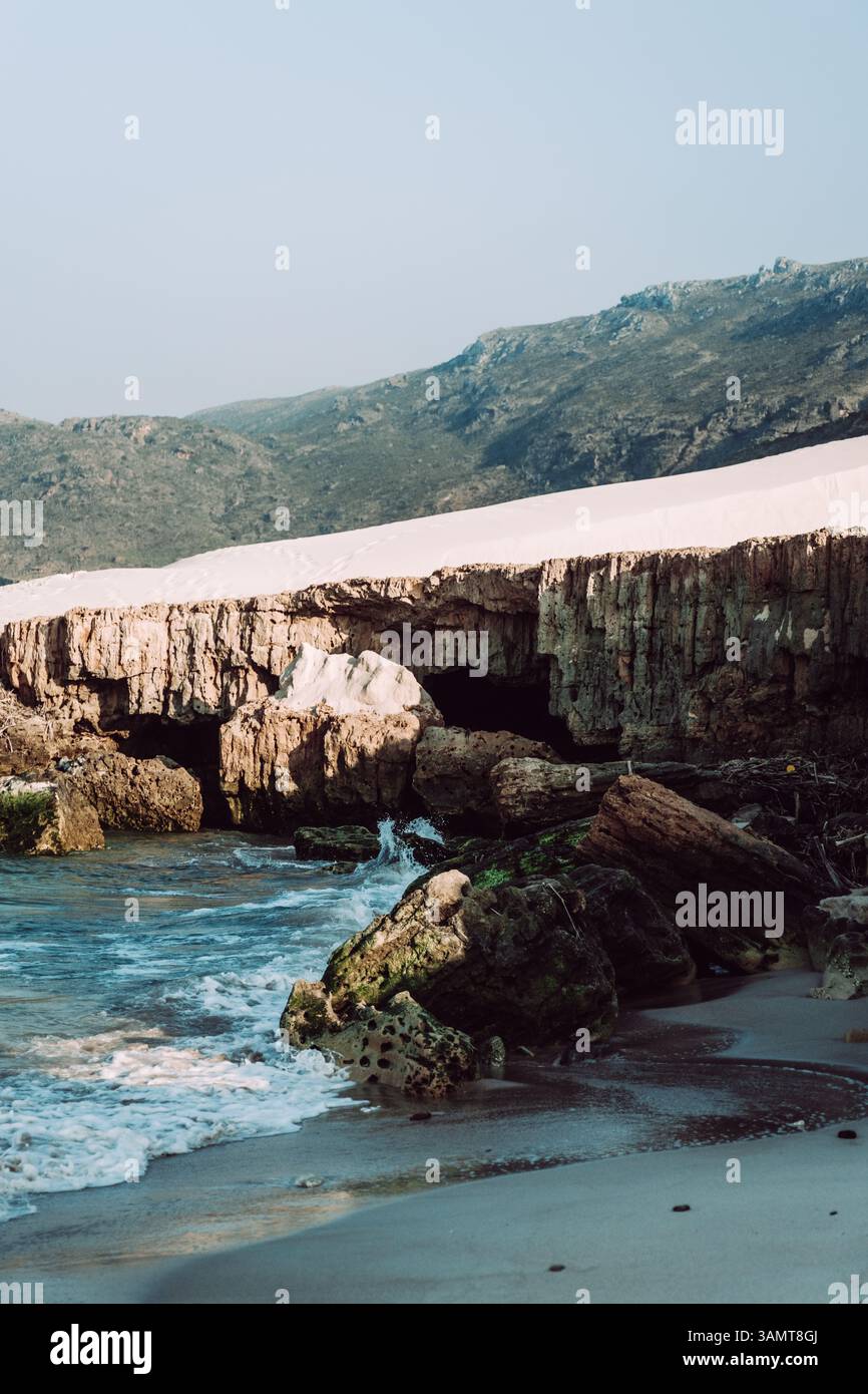 Waves crash against rocky shoreline beneath sand dunes at Delisha Beach ...