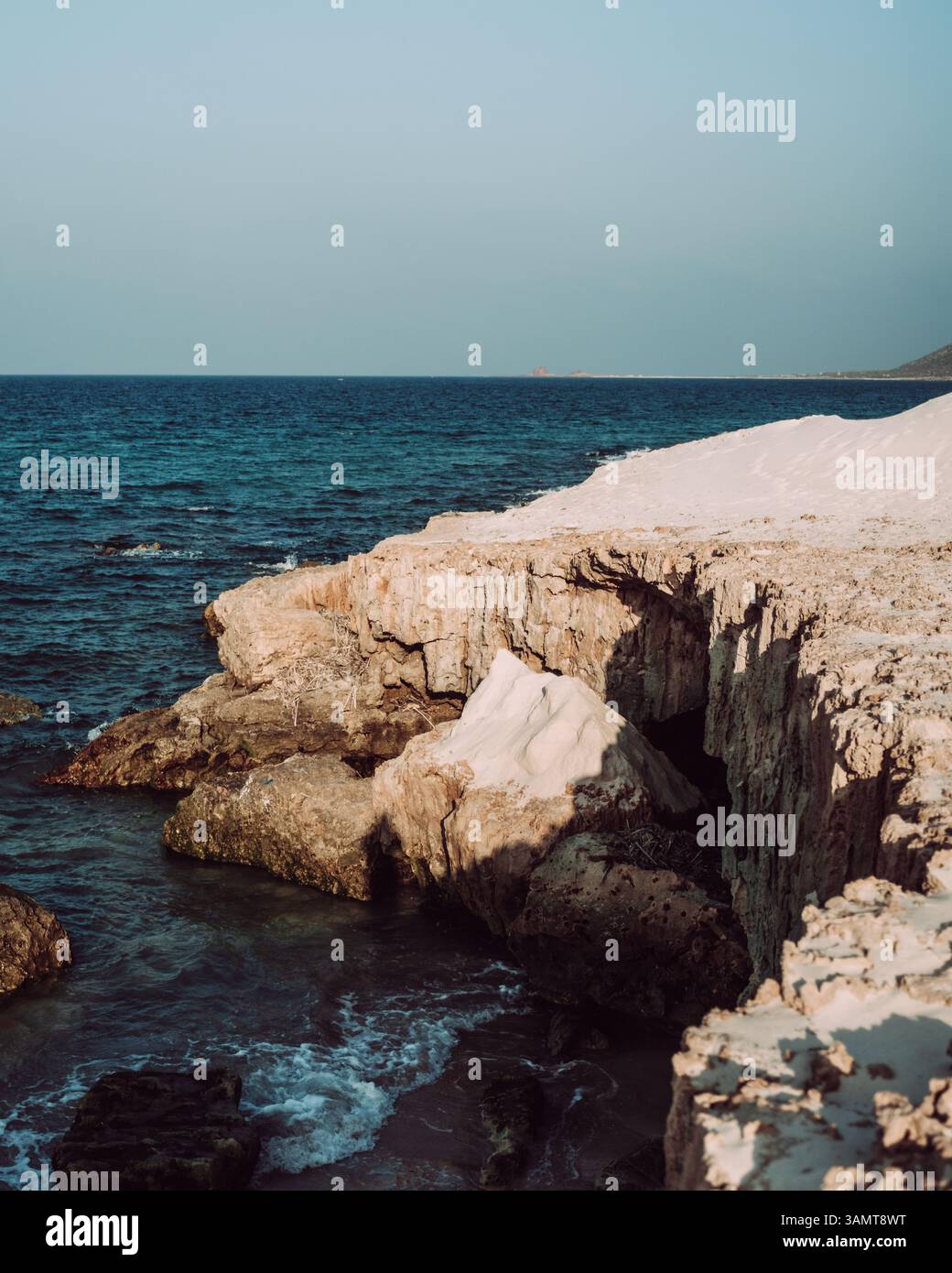 Waves crash against rocky shoreline beneath sand dunes at Delisha Beach ...