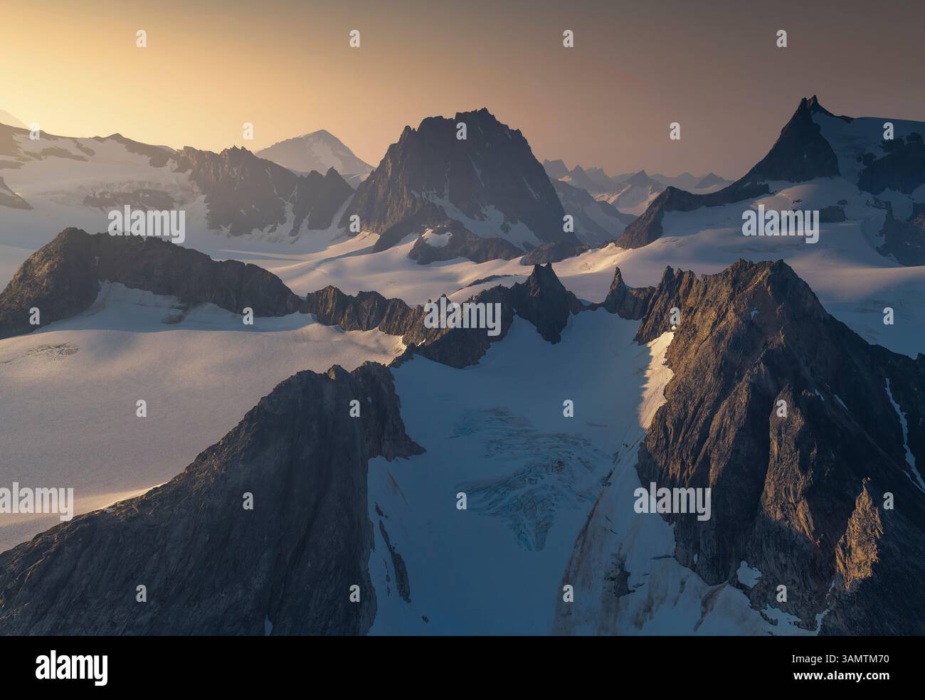 Aerial view of dramatic sunset over snow-capped mountains and glaciers ...