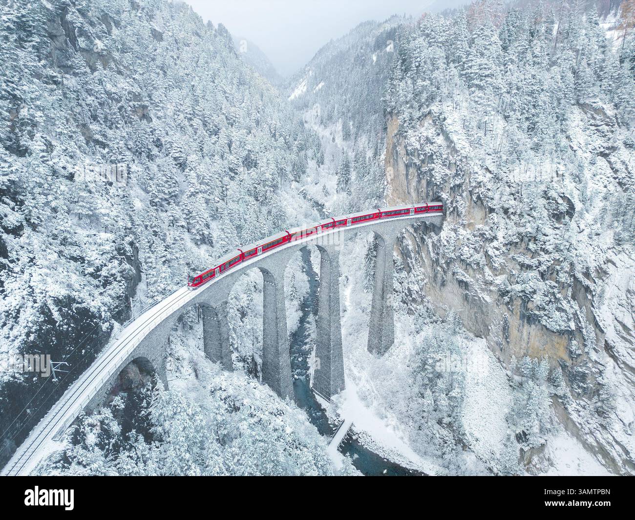 Aerial view of landwasser viaduct with a red train crossing over snowy ...