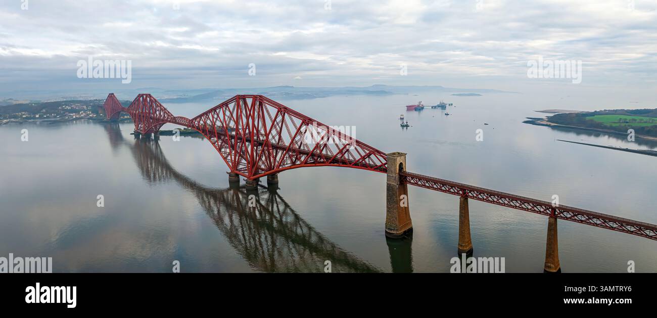 Aerial view of the iconic Forth Rail Bridge at sunset with reflections ...