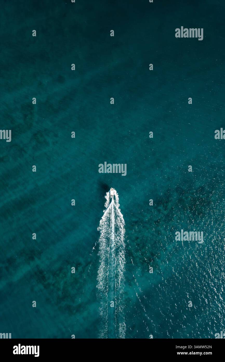 Aerial view of a boat driving in clear blue water, top down perspective ...