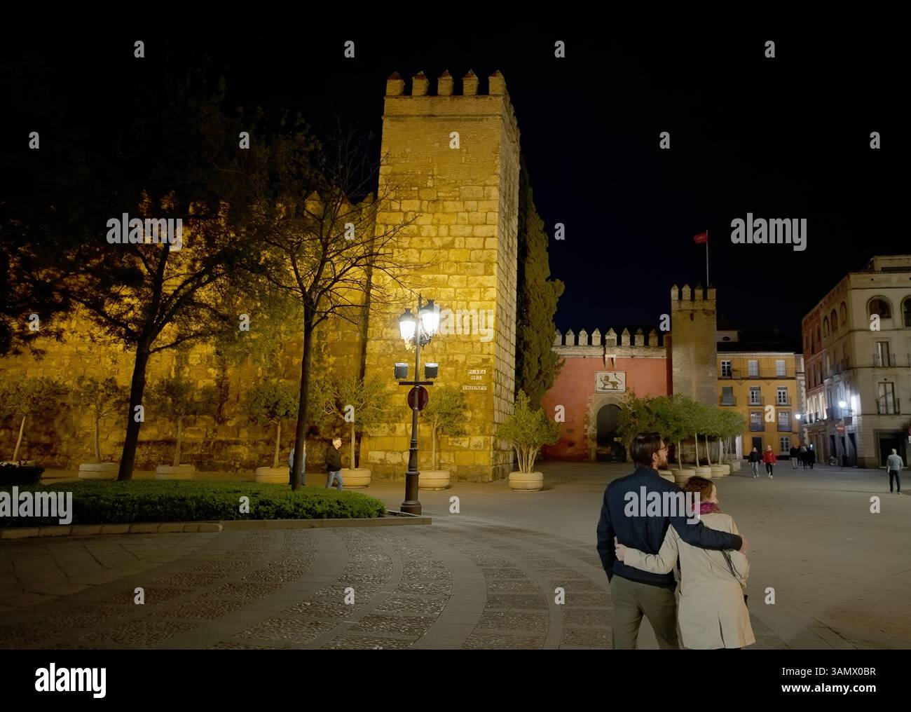 Tourists hugging at night in Seville, enjoying the view of Puerta de ...