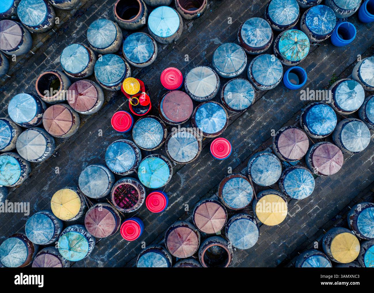 Aerial view of vibrant circles of clay urns and a worker with a yellow ...