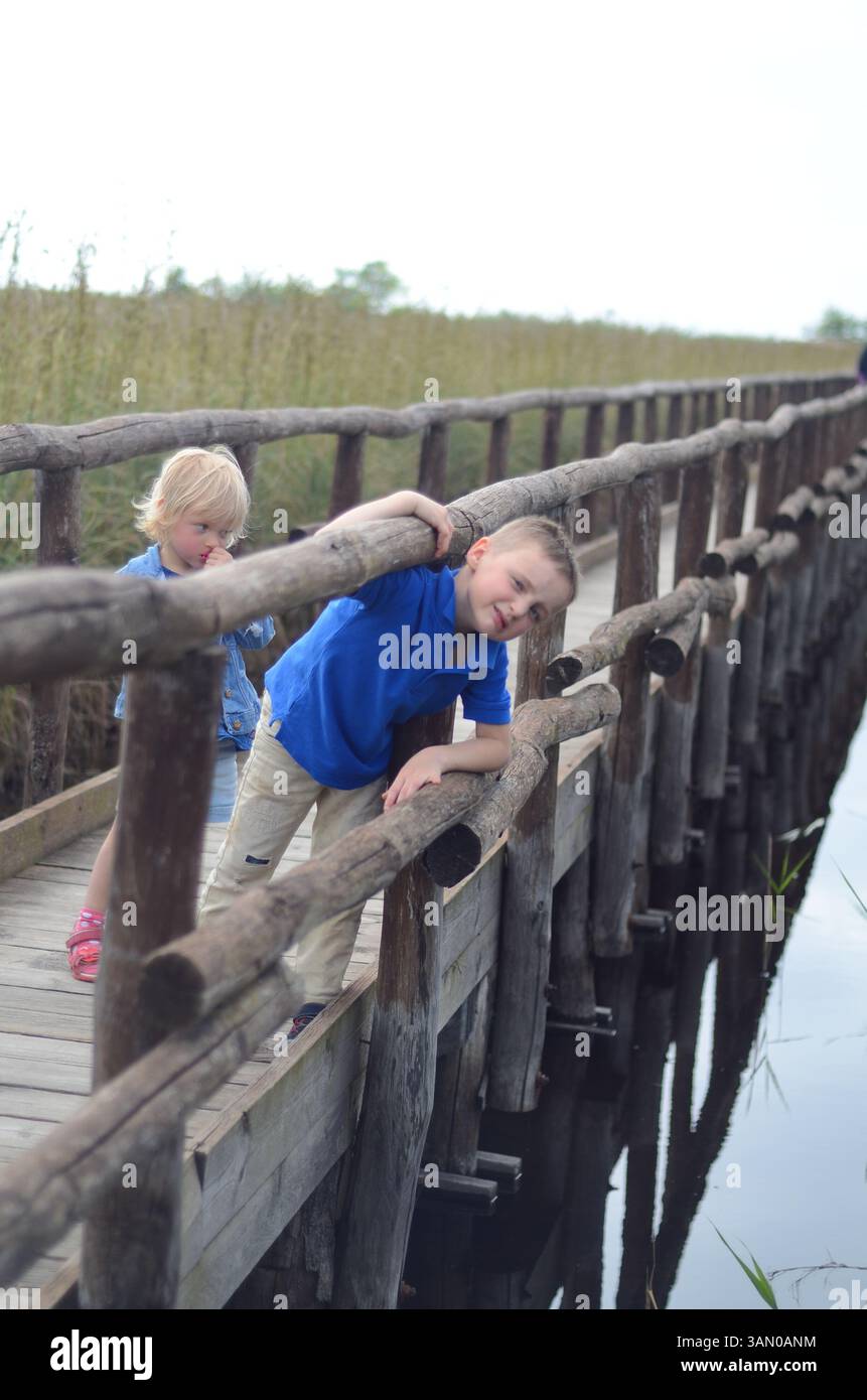 Children are playfully exploring a wooden boardwalk bridge over water ...