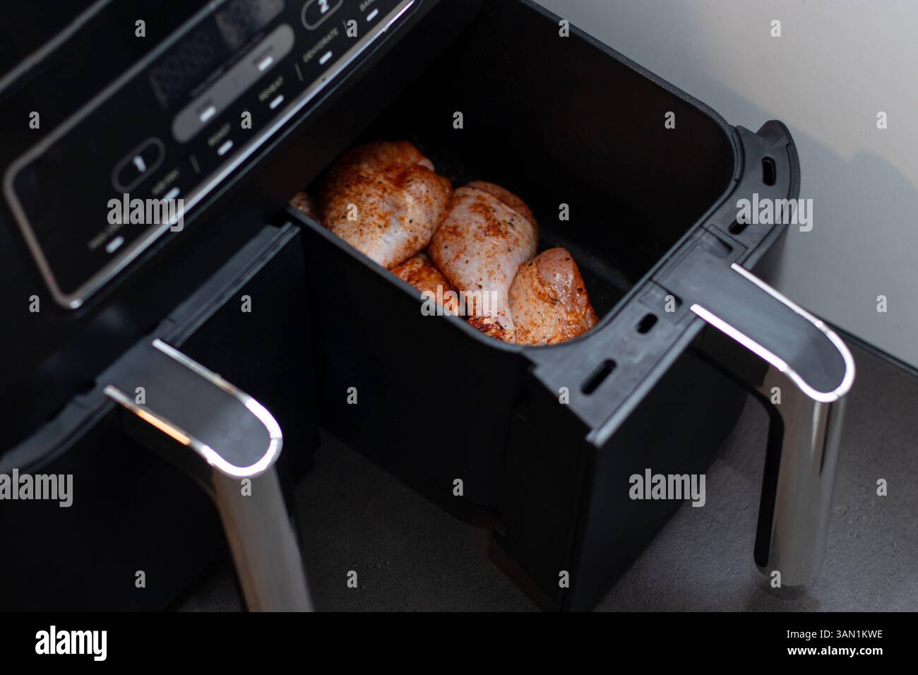 Close up an open air fryer with raw and seasoned chicken drumsticks ...