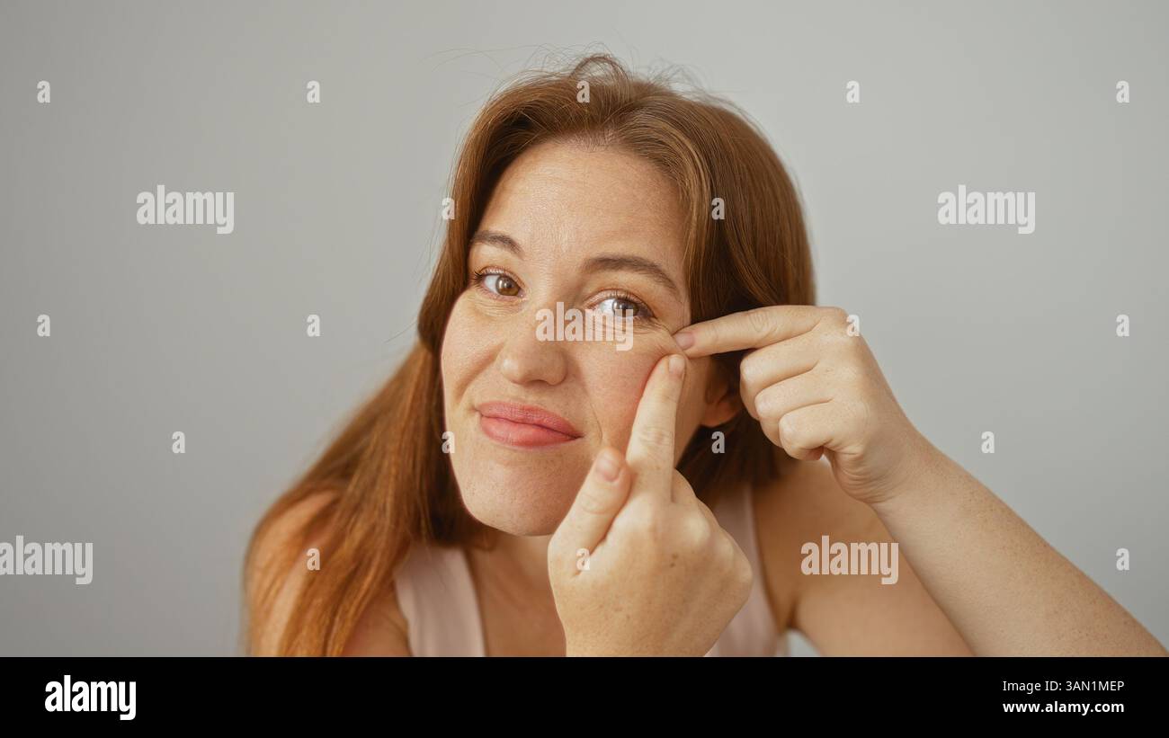 Woman squeezing pimple on face with fingers against white background ...