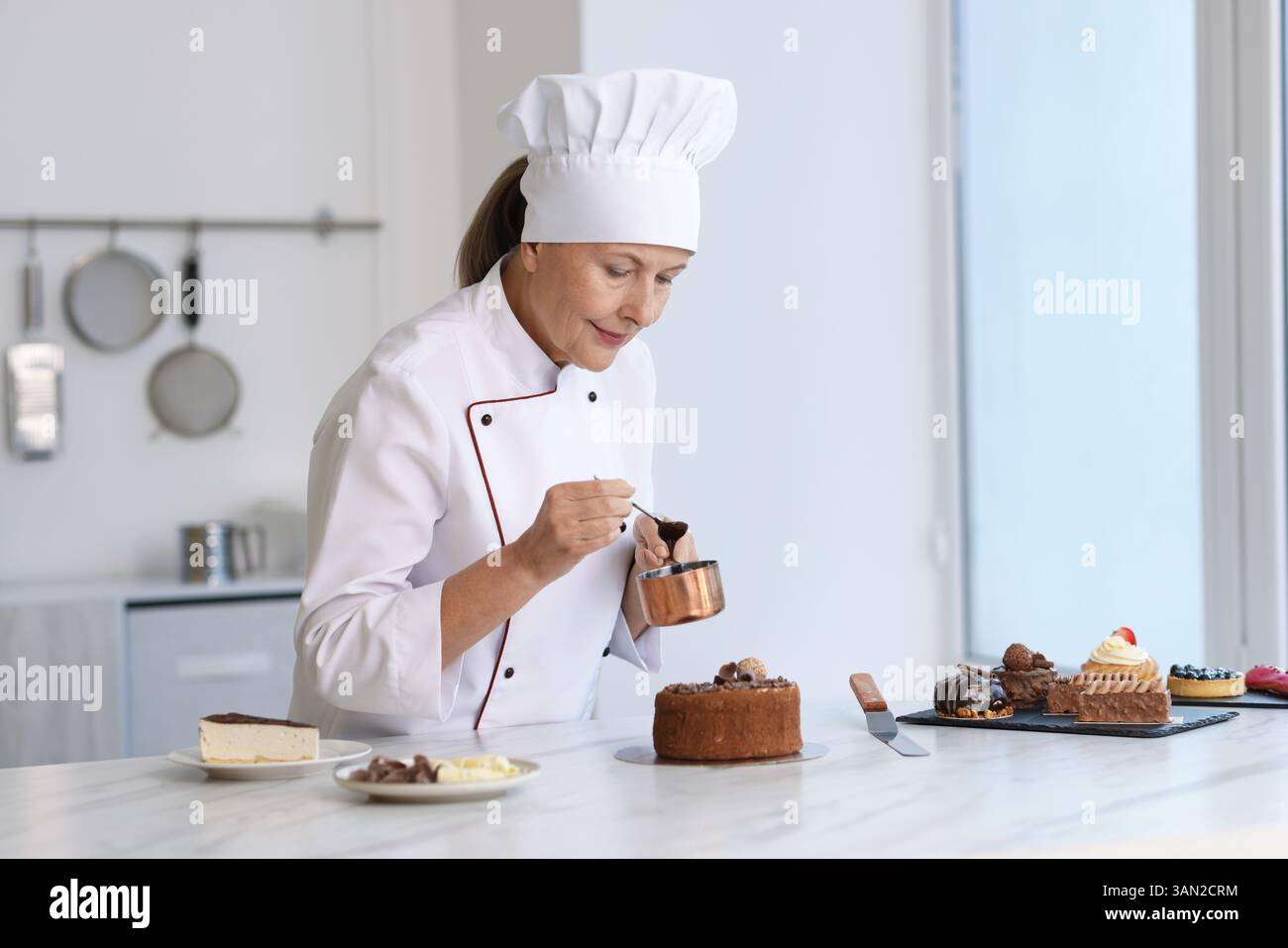 Senior pastry chef decorating cake with melted chocolate at table in ...