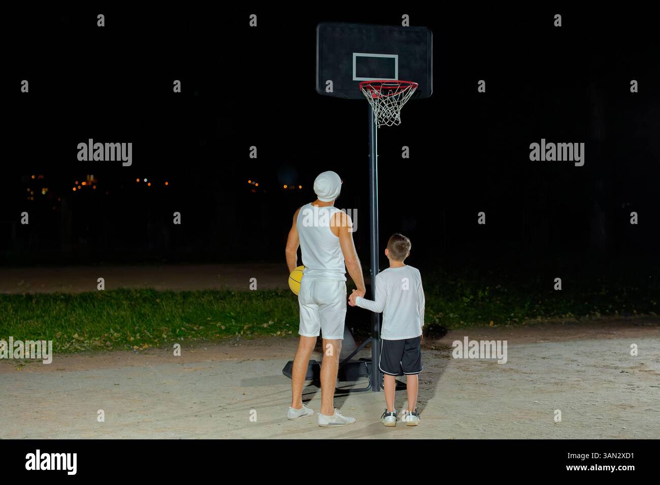 A father and his young son walk hand in hand toward a lit outdoor ...