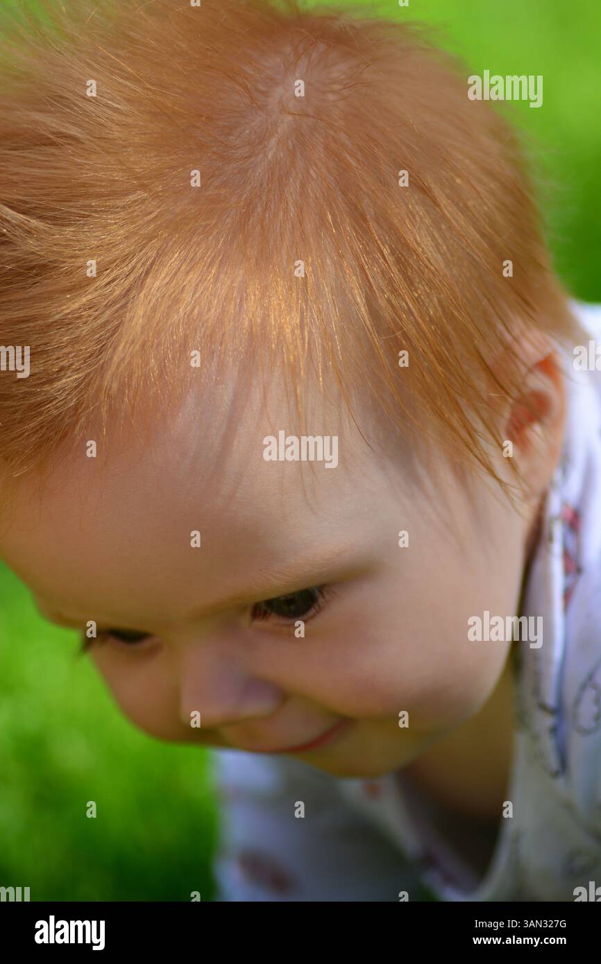 Red hair baby girl smiling close portrait in a back yard . Toddler girl ...