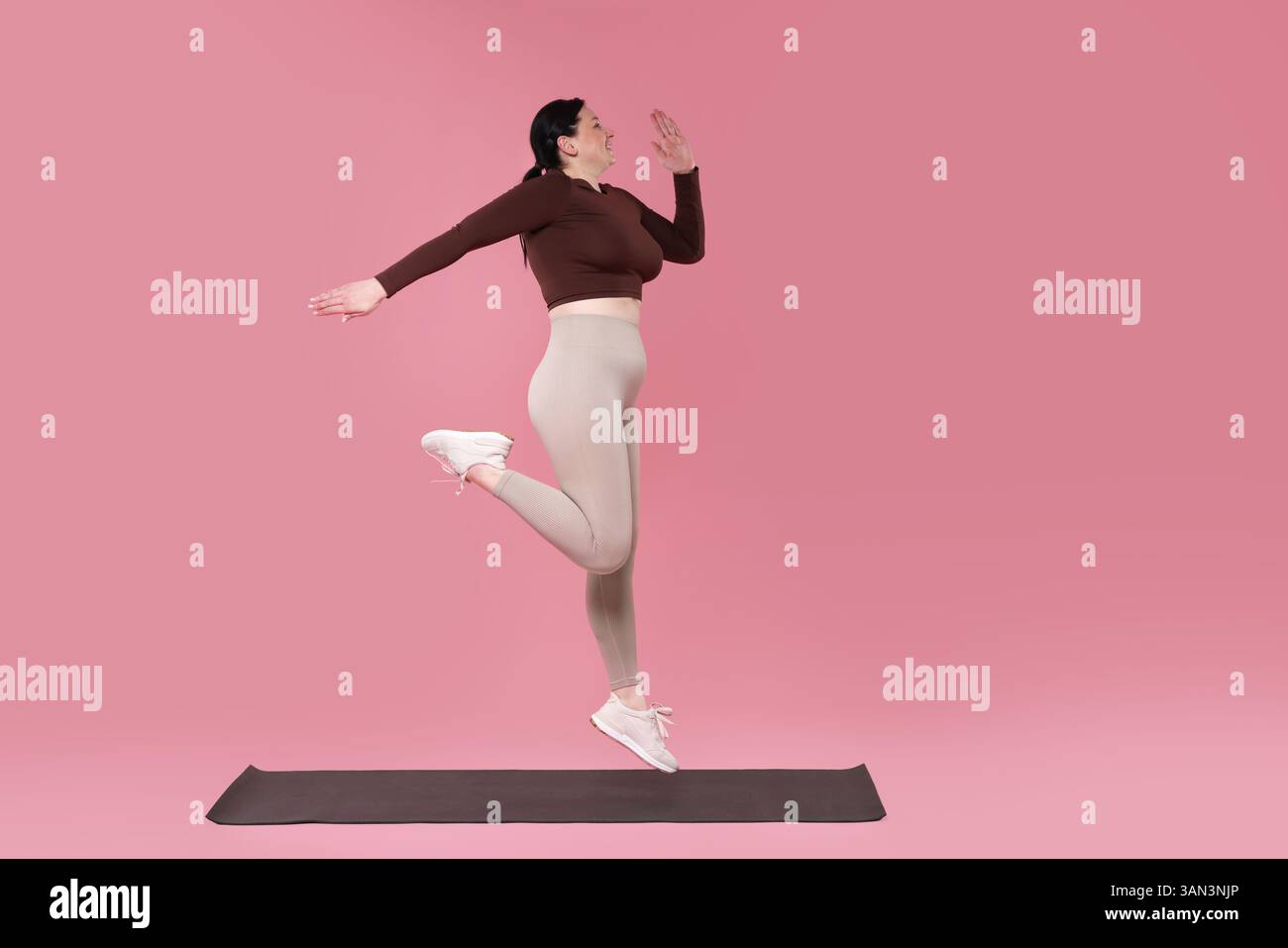 Plus size woman in gym clothes exercising on pink background Stock ...