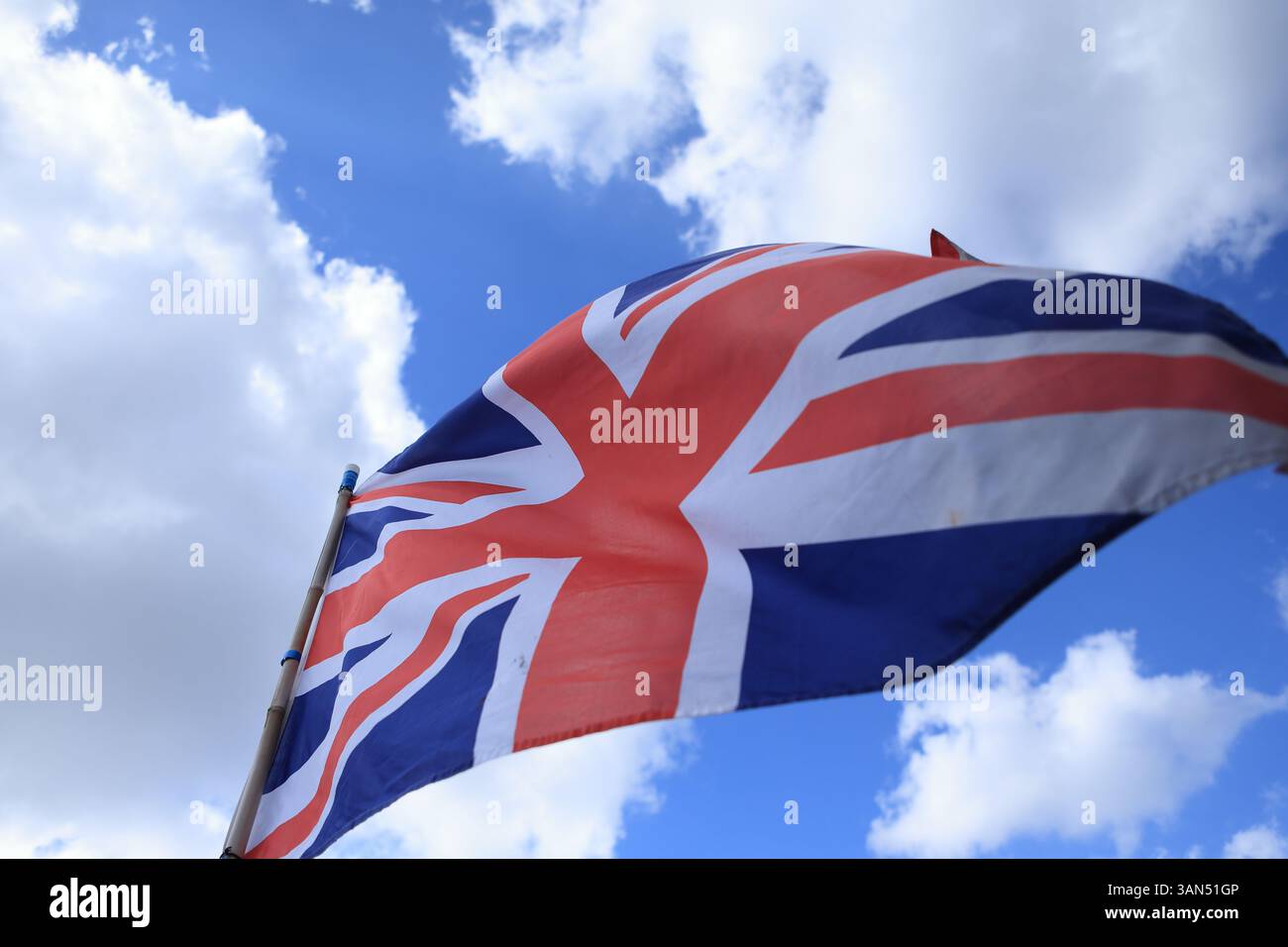 UK Union Jack flag flaps in wind against blue sky with white clouds ...