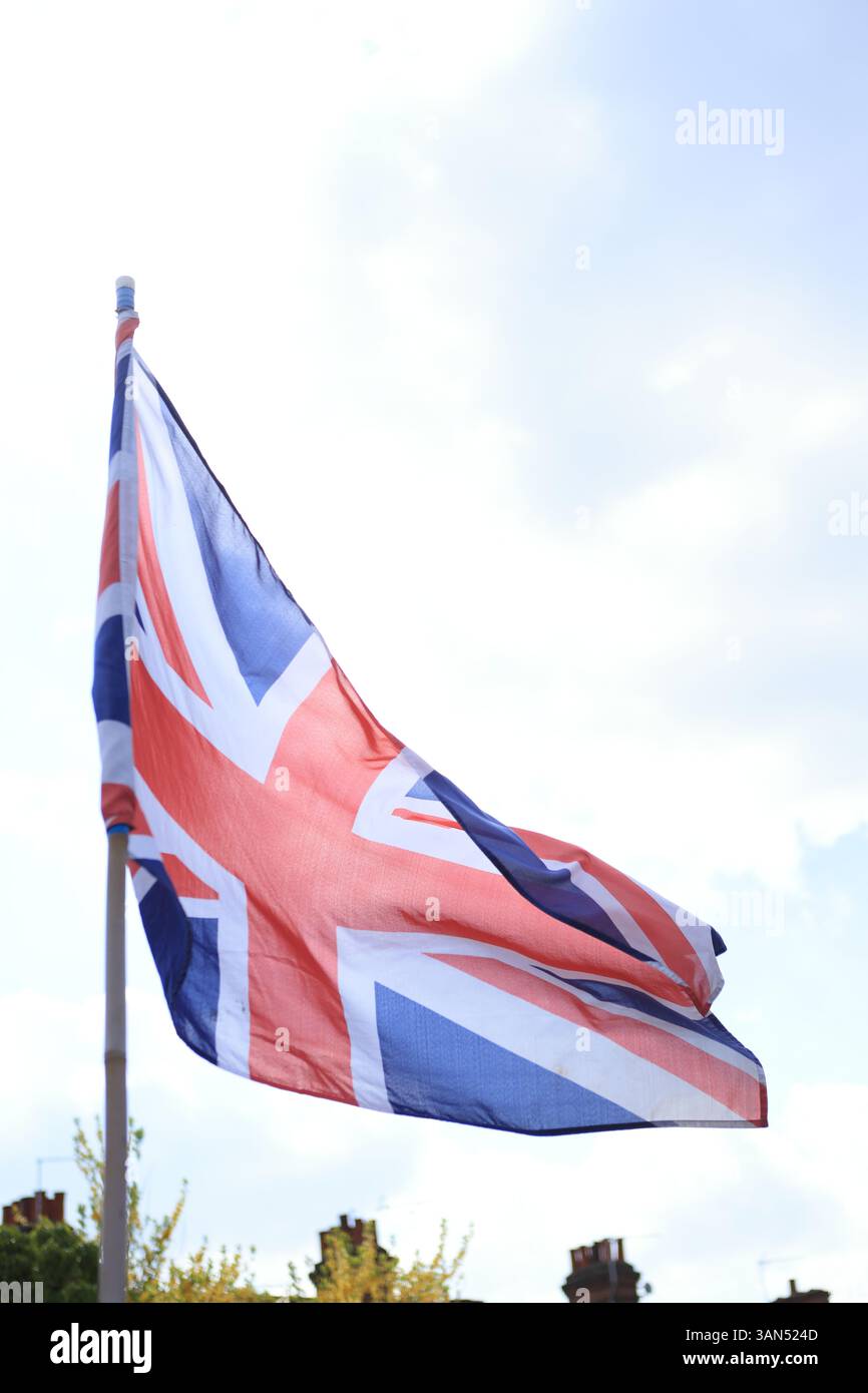 UK Union Jack flag flaps in wind against blue sky with white clouds ...