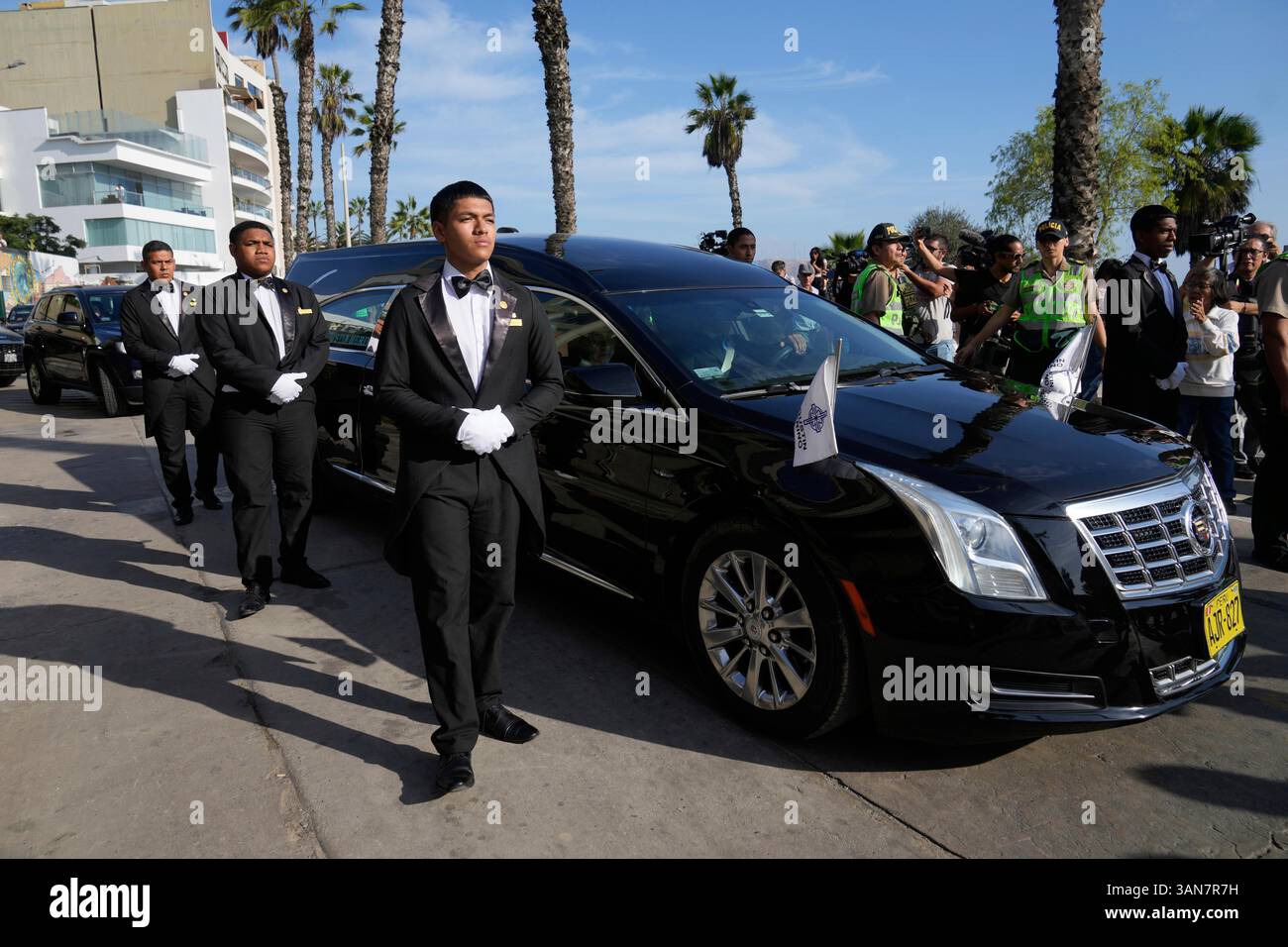 Funeral workers stand beside a hearse driving the coffin of Peruvian ...