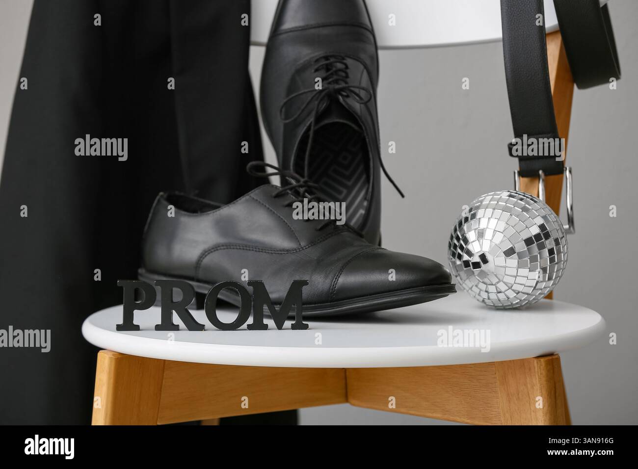 Word PROM with male shoes, blazer and disco ball on chair against white ...