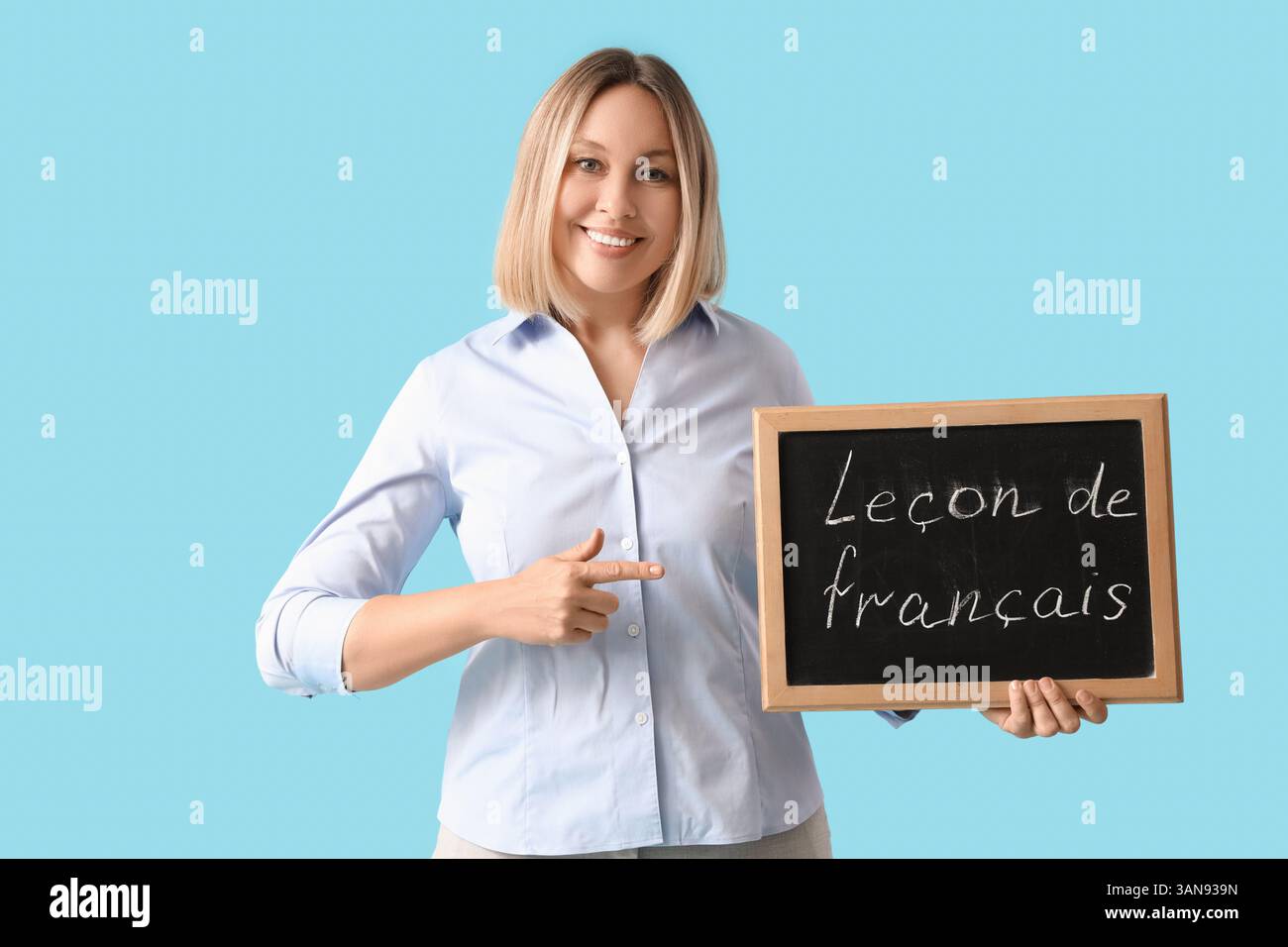 Female French language teacher pointing at small blackboard on blue ...